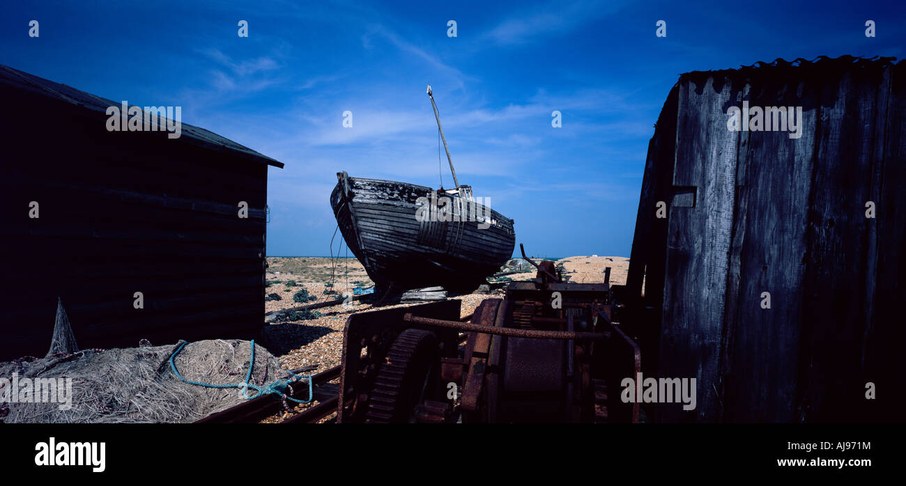 Old wooden hulled fishing boat with winch and sheds on shingle beach ...