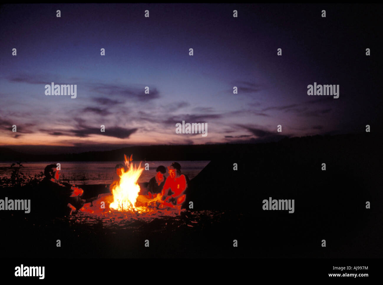 Friends sitting around campfire Stock Photo - Alamy
