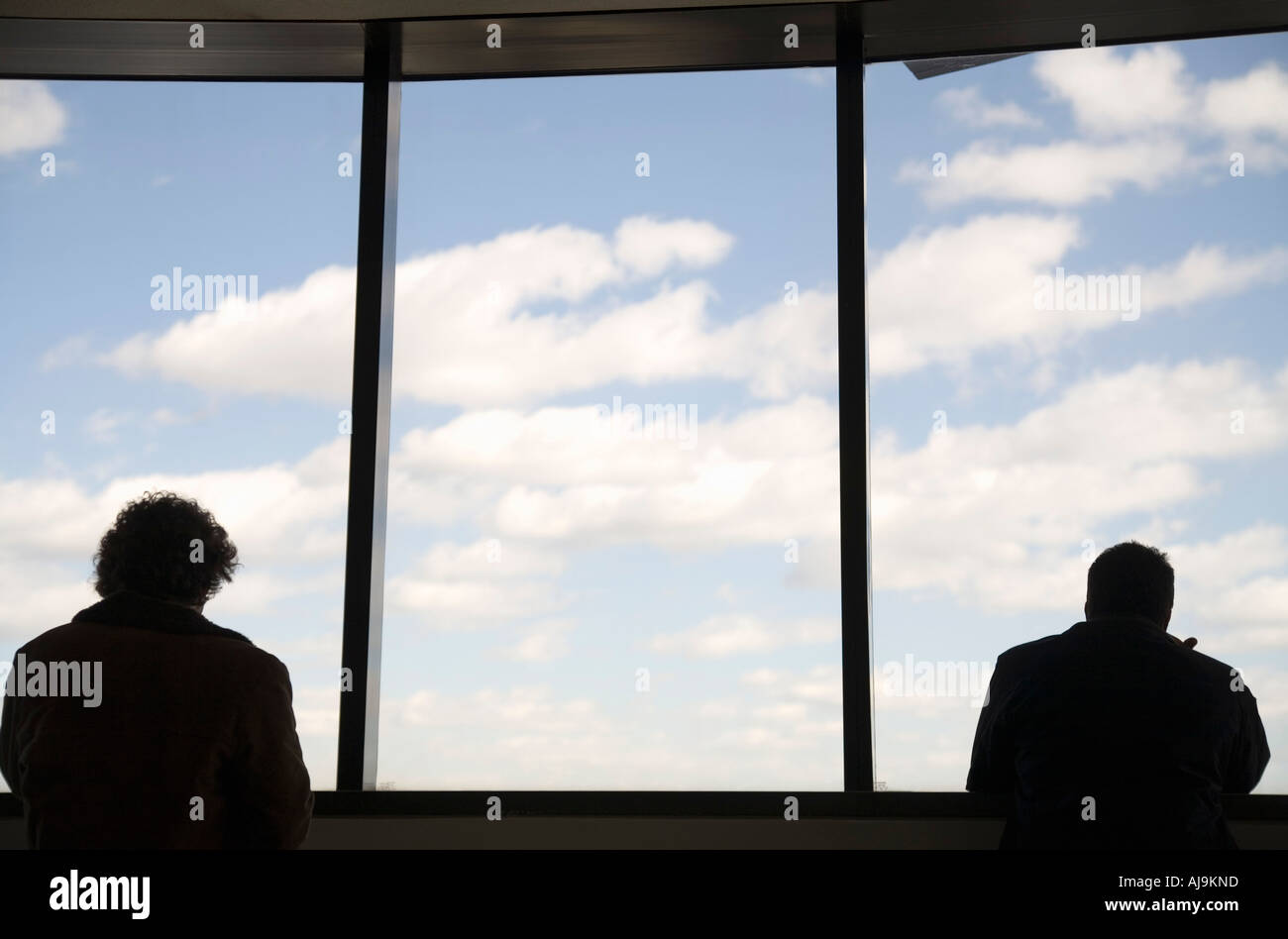 Two people looking out large windows Stock Photo - Alamy