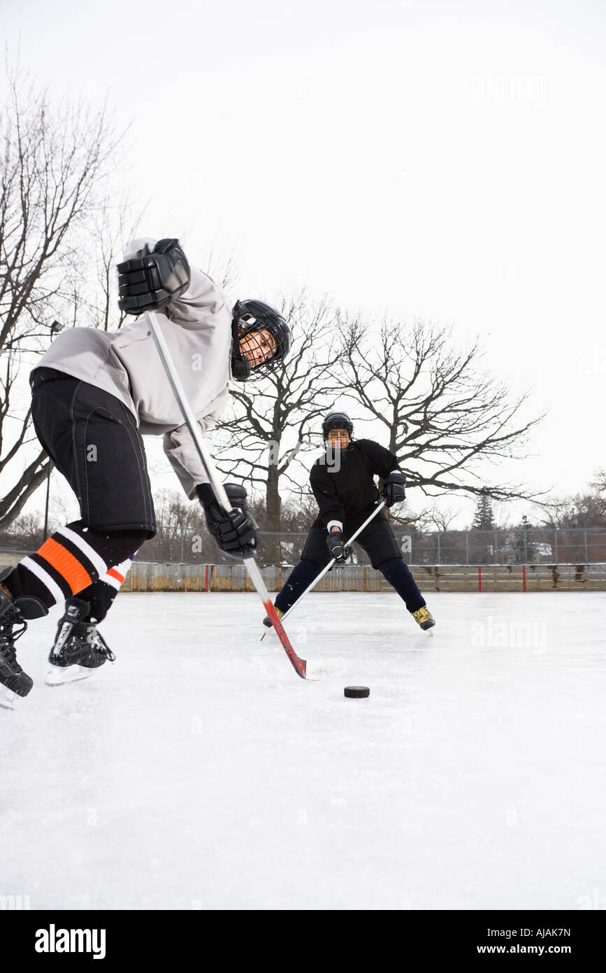 Two boys in ice hockey uniforms skating on ice rink moving puck Stock ...