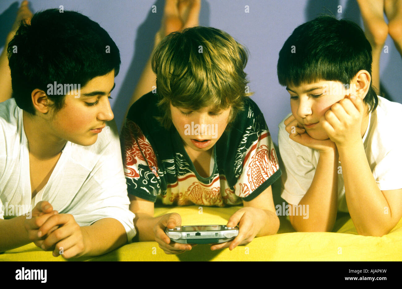 a young boy playing with his gameboy while his two friends are watching ...