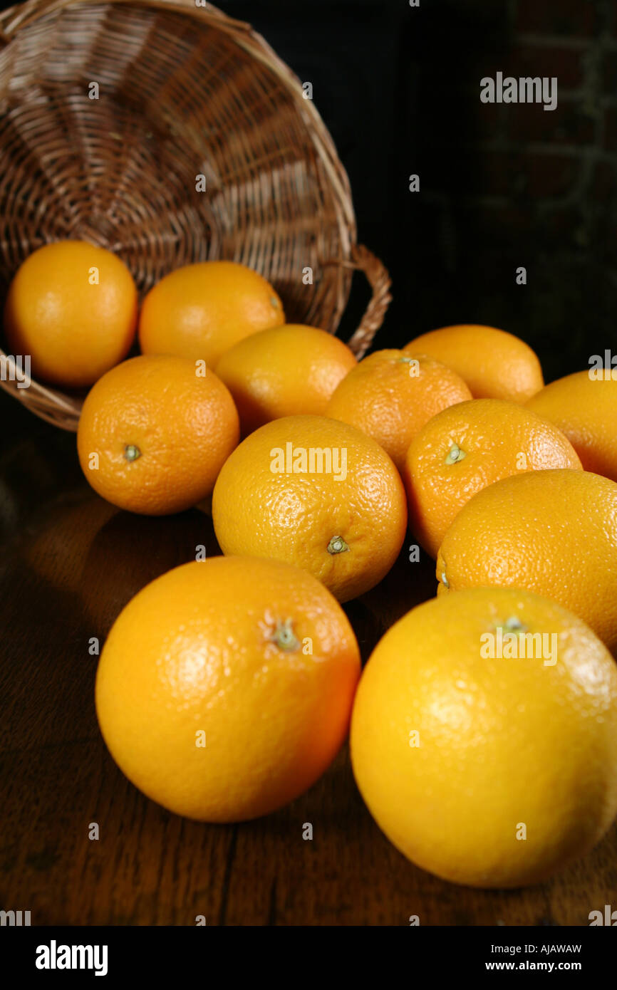 several oranges spilling from an upturned basket on dark wood surface ...