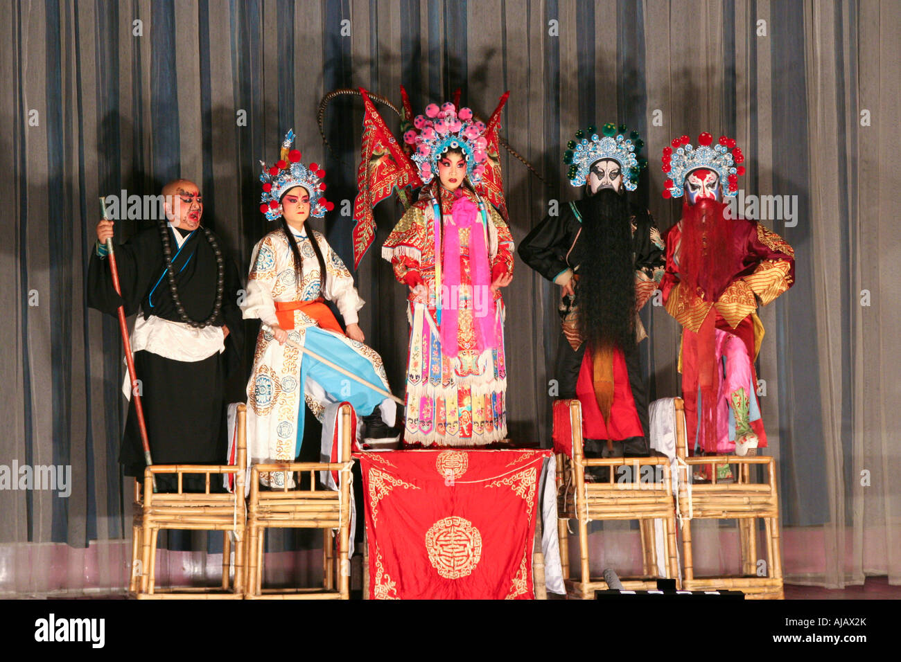 Opera actors dressed in traditional clothing are all standing on chairs ...