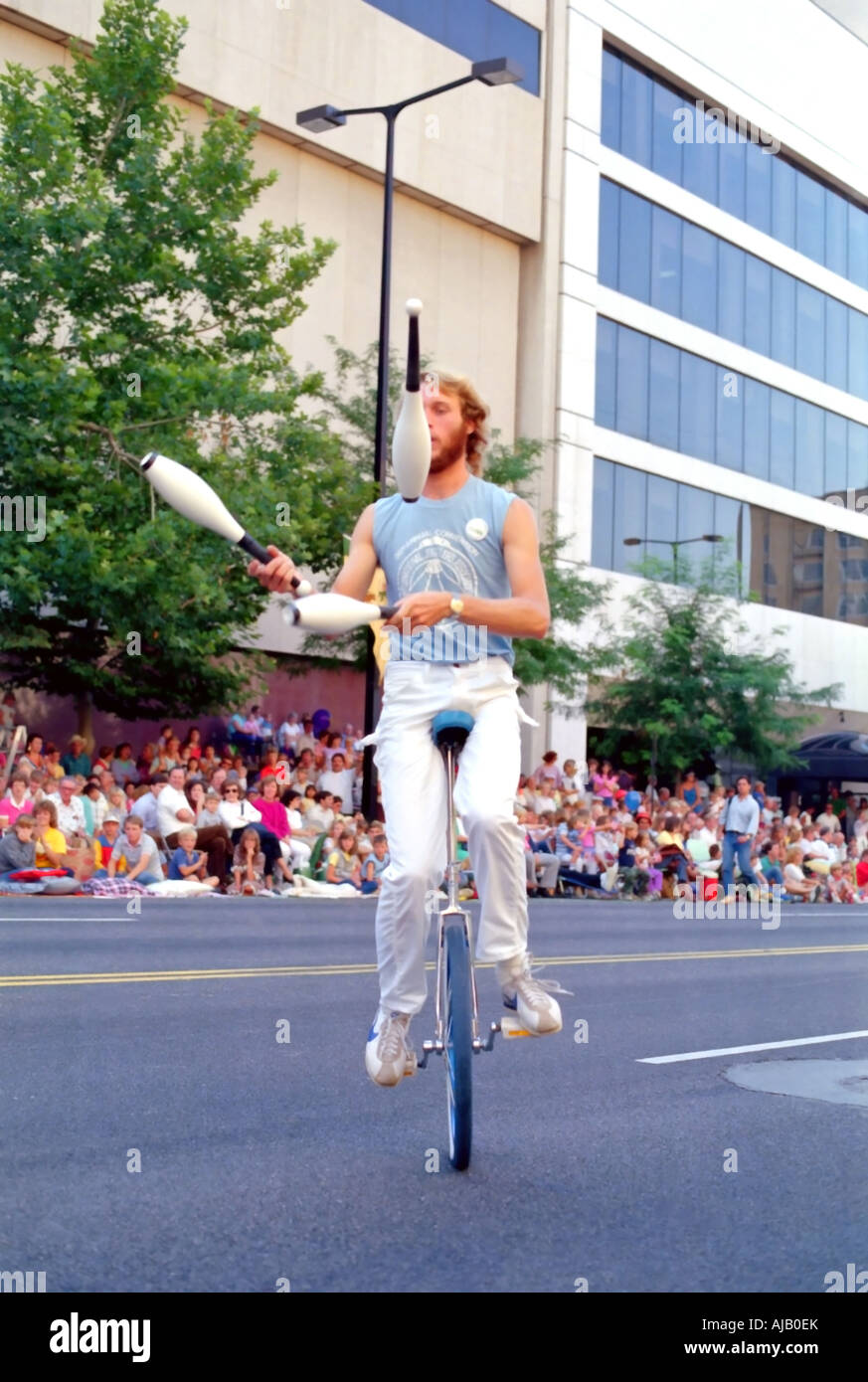 A juggler juggles while riding a unicycle while a crowd looks on at ...