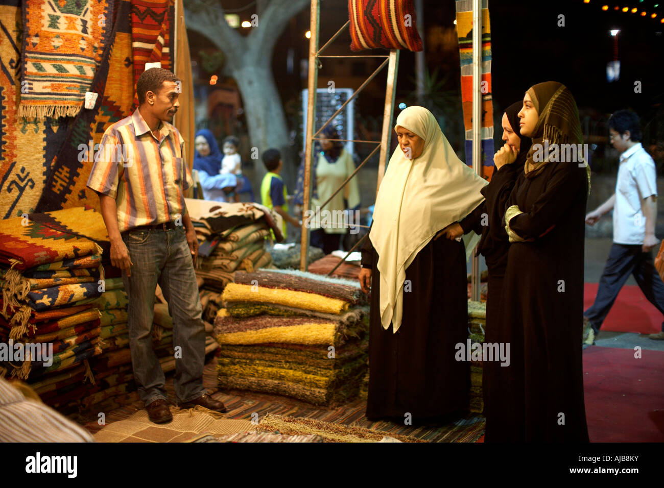 Muslim women with head scarfes looking at carpets on display at night ...