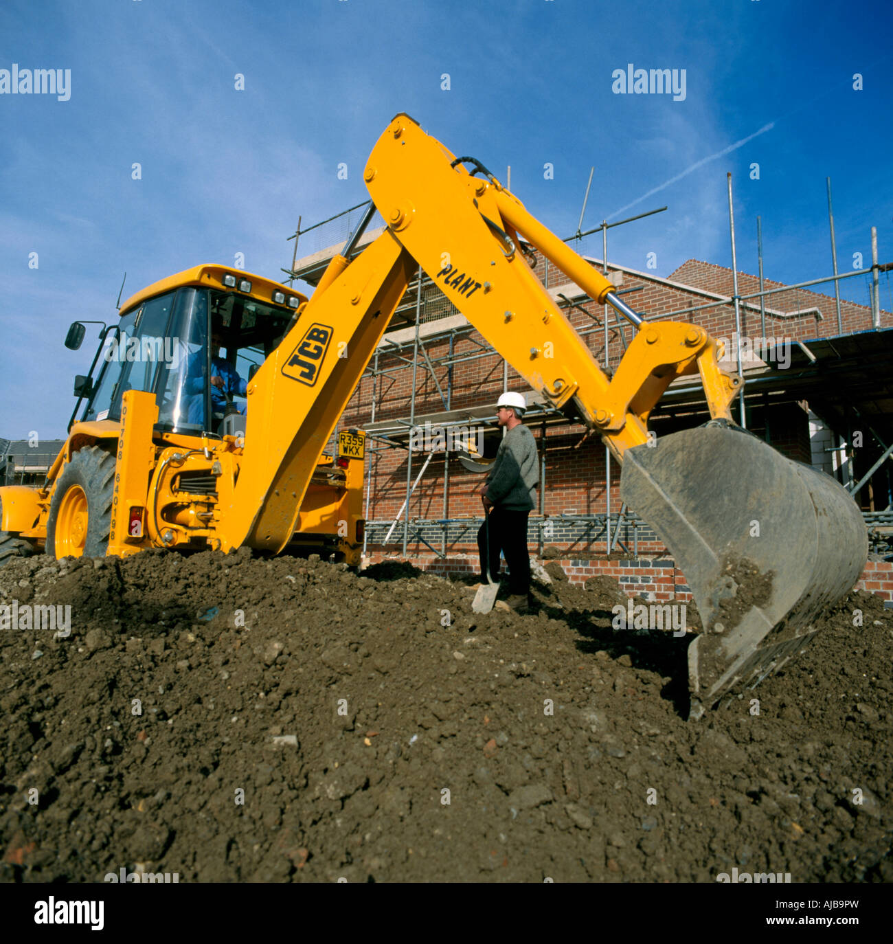 JCB excavator plant machinery from low angle digging spoil with worker ...