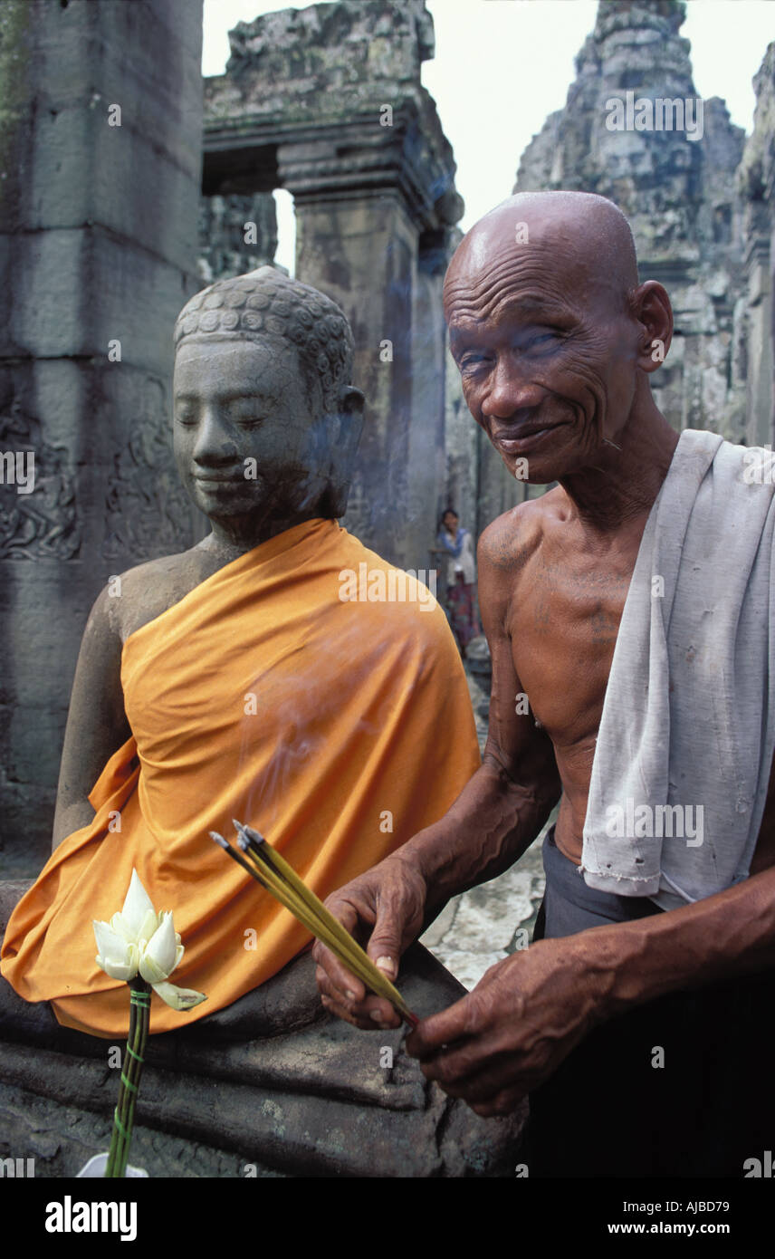 ANGKOR CAMBODIA Friendly monk tending to a saffron robed Buddha image ...
