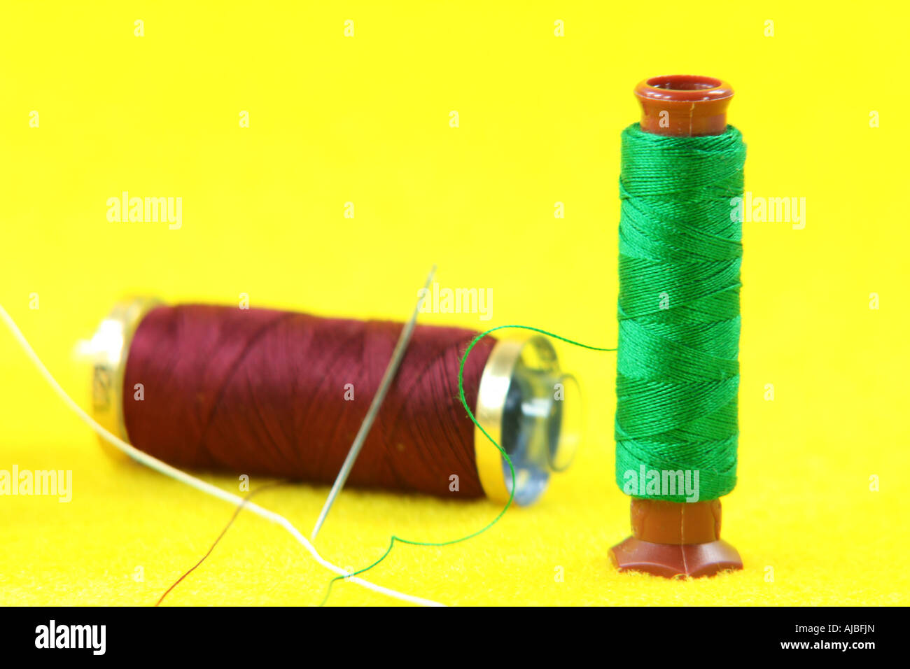 green string roll needle with redish string in yellow background sewing ...