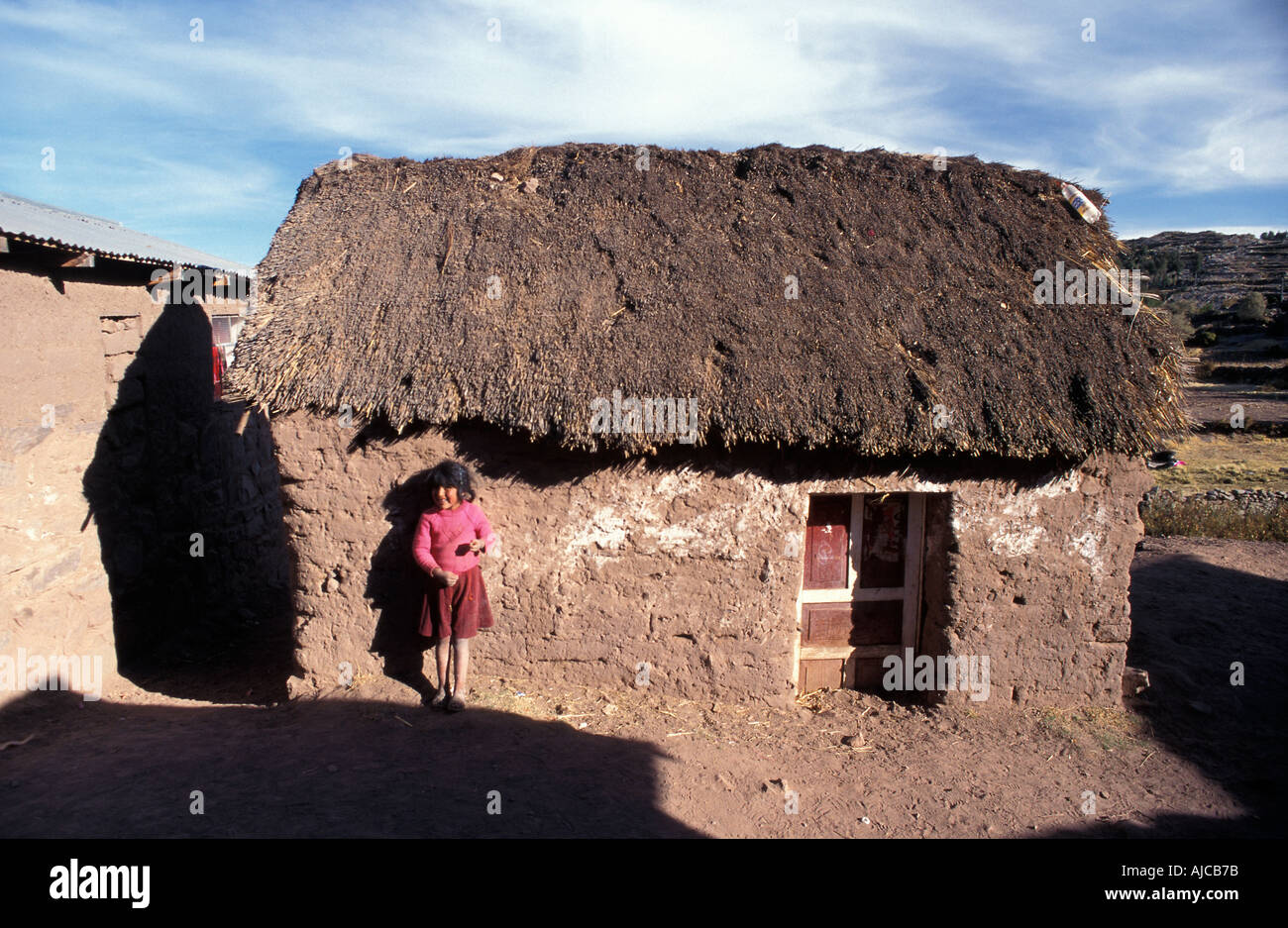 Youngster with a drop spindle re spinning thread outside an adobe home ...