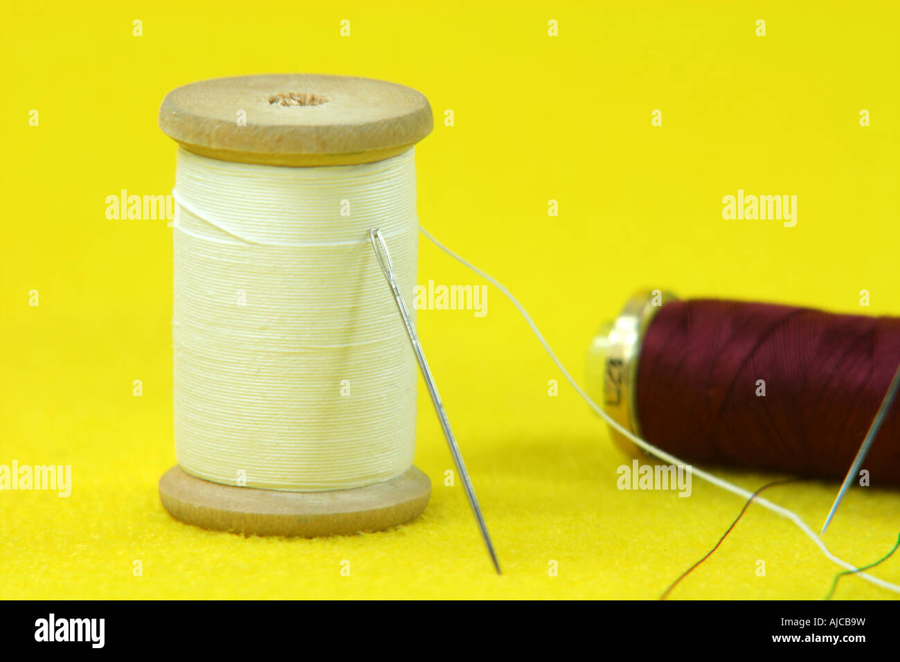 white string roll needle with redish string in yellow background sewing ...