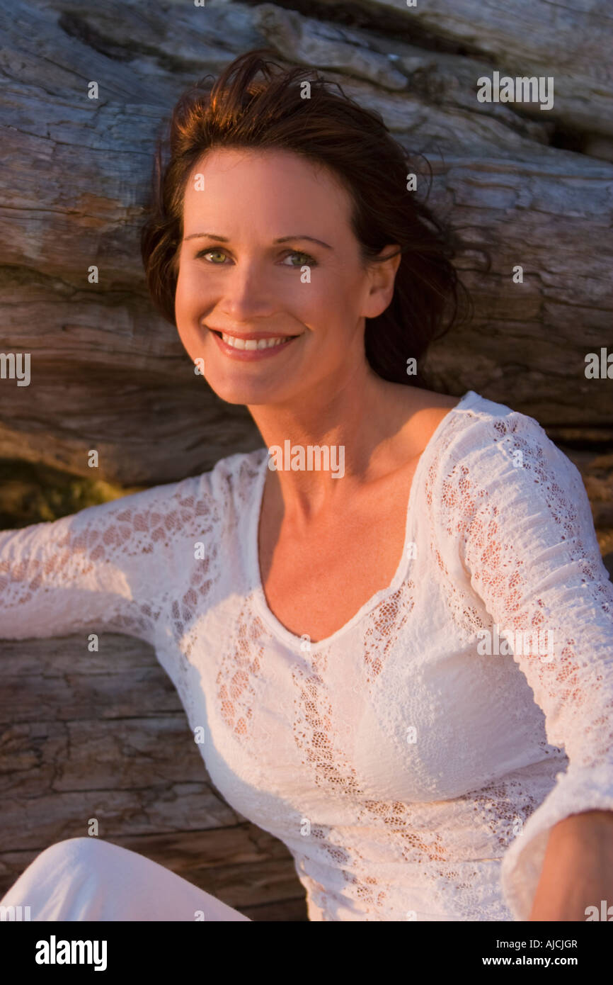 Woman at the beach portrait by a log at sunset Stock Photo - Alamy