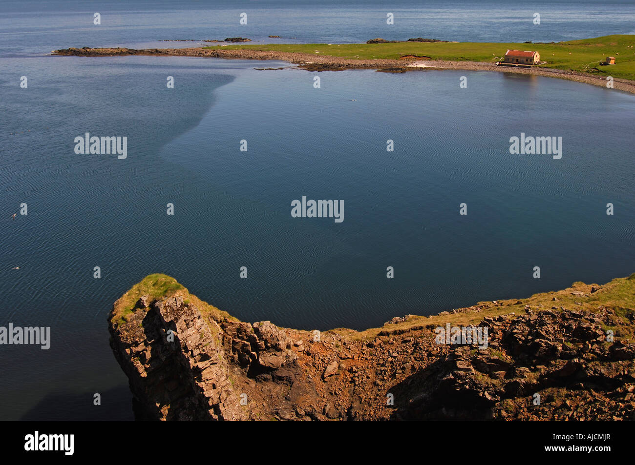 Rugged cliff top and old farm buildings on the shores of Reydarfjordur ...