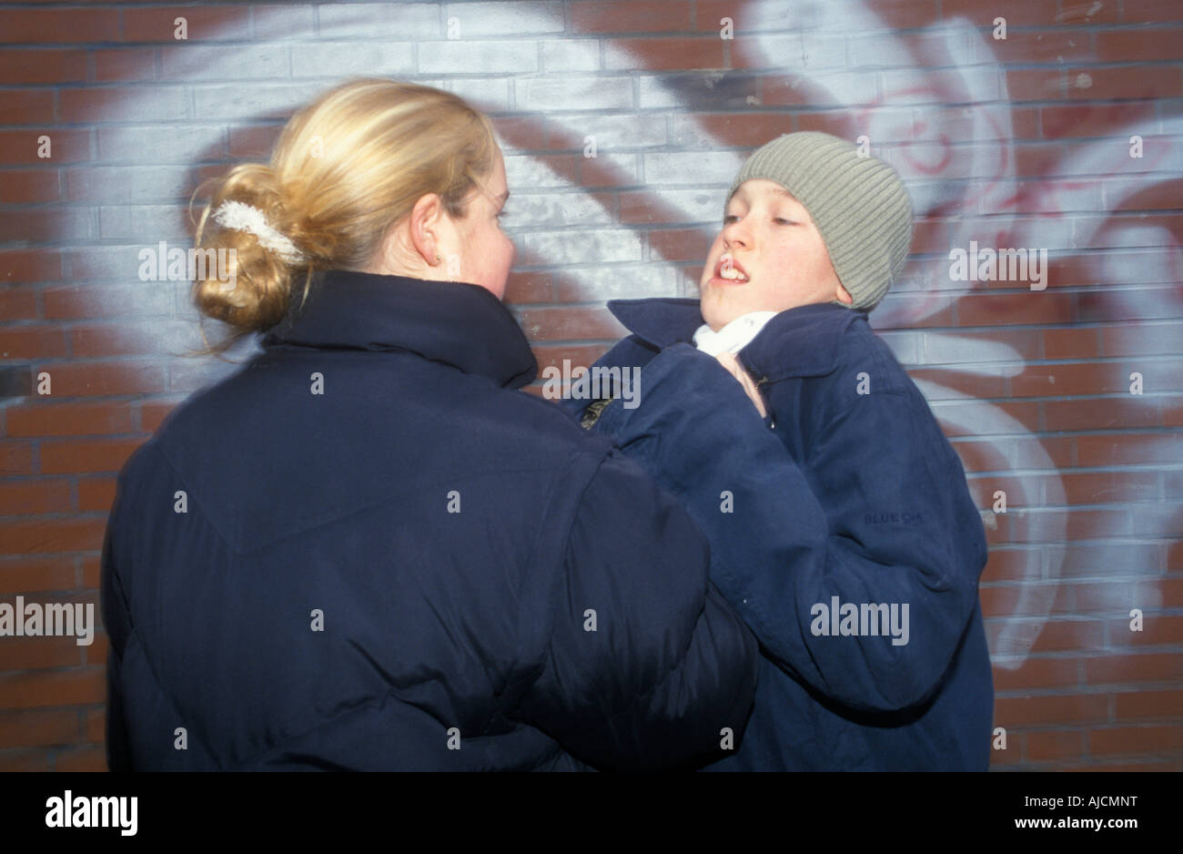 a teenage girl is pushing a younger boy against a wall choking him ...