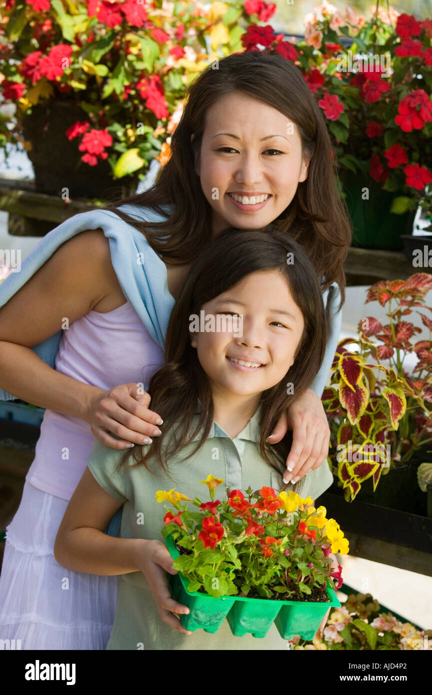 Mother with daughter holding young flowers in plant nursery, portrait ...