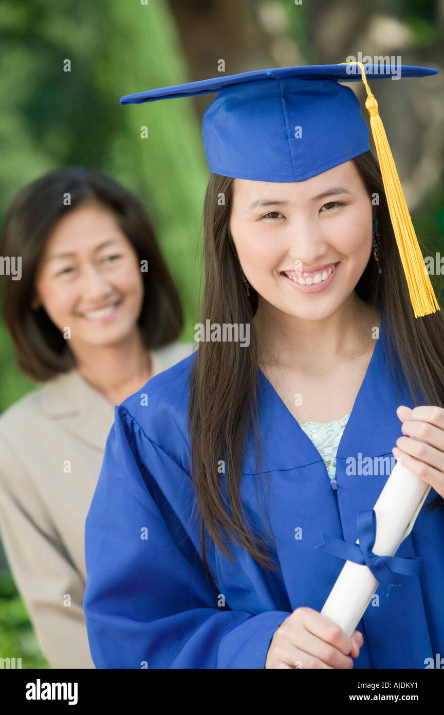 Graduate holding diploma with mother behind, outside, portrait Stock ...