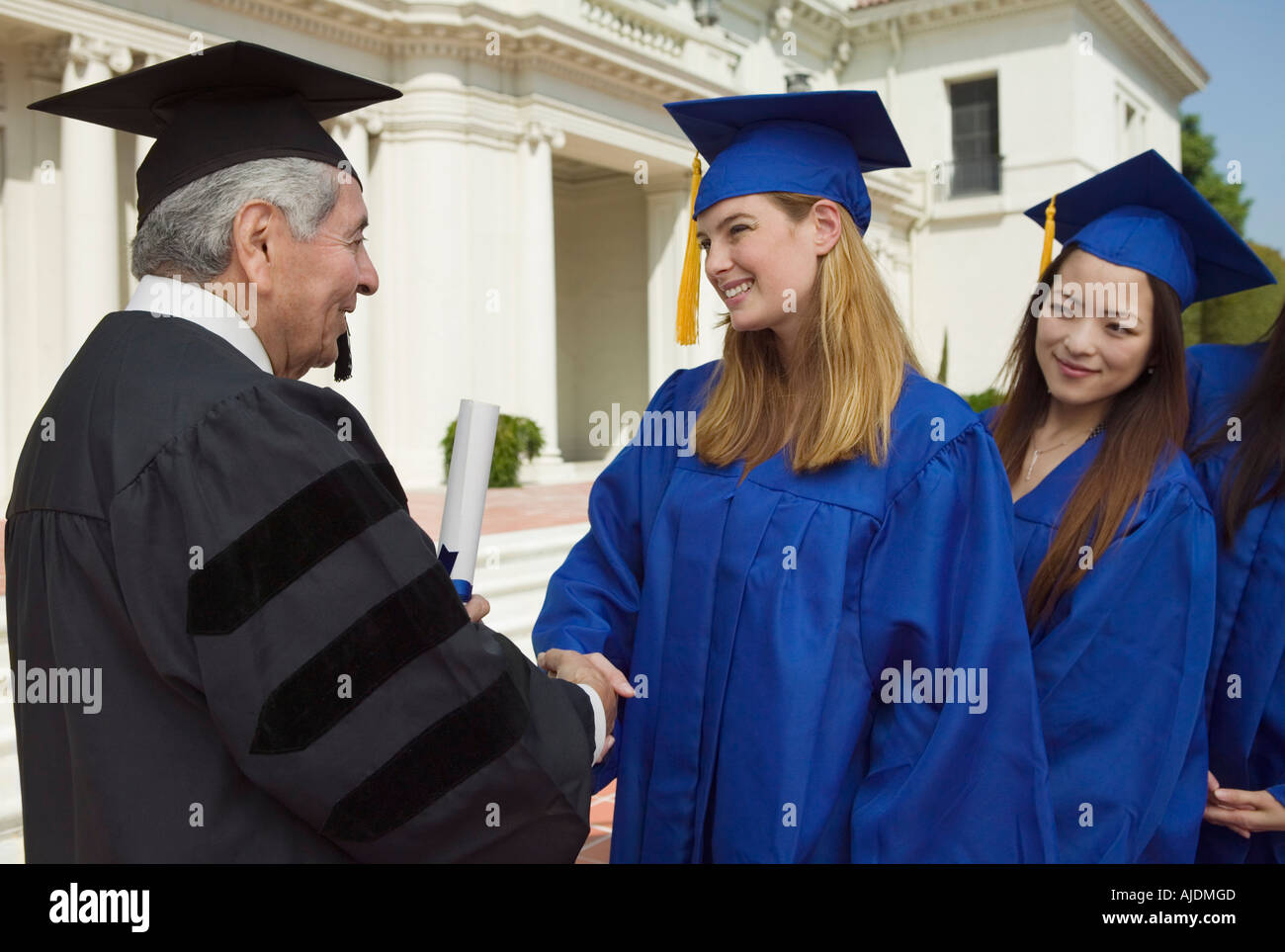 Graduates in line to shake hand of dean outside university, side view ...
