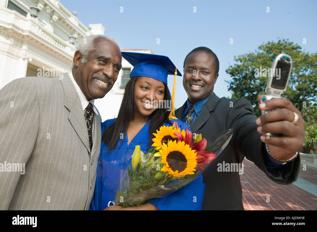 Graduate with father and grandfather taking picture with cell phone ...