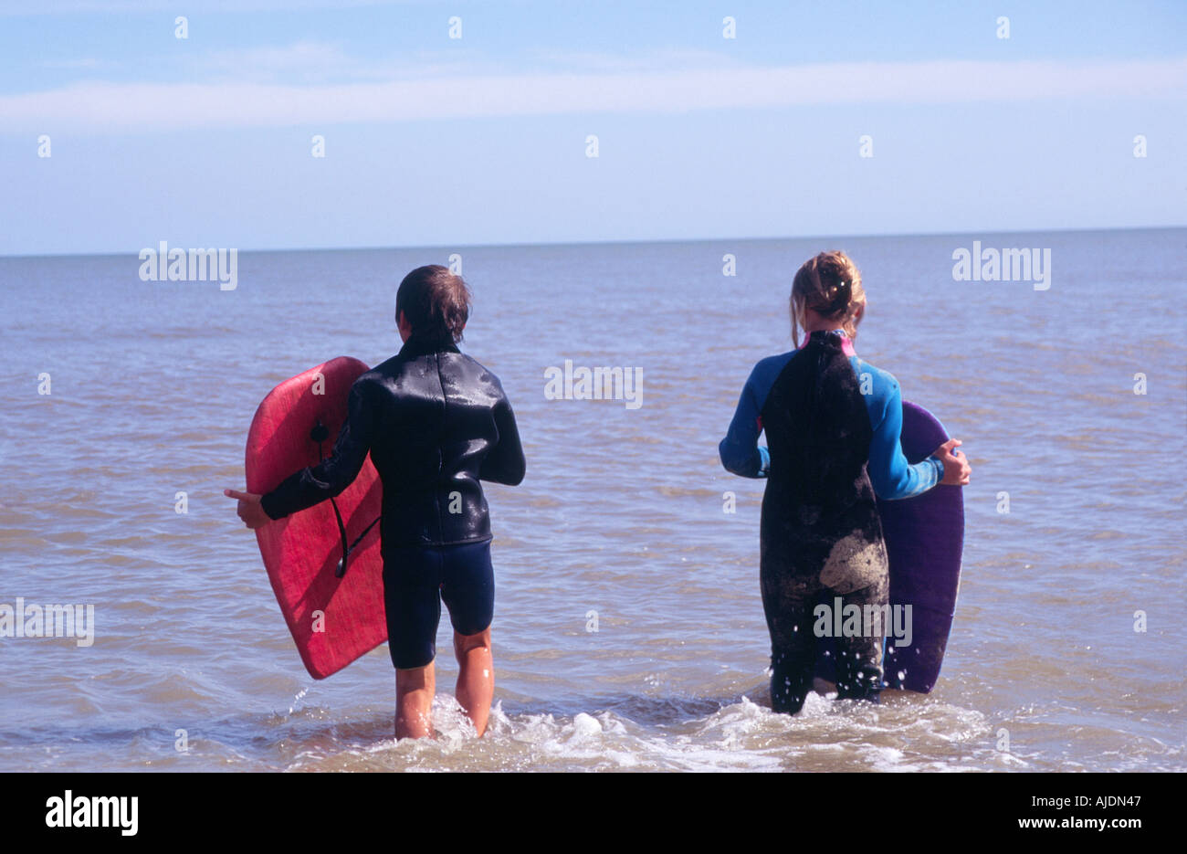 Two childen in black wet suits body boarding sea waiting for a wave ...