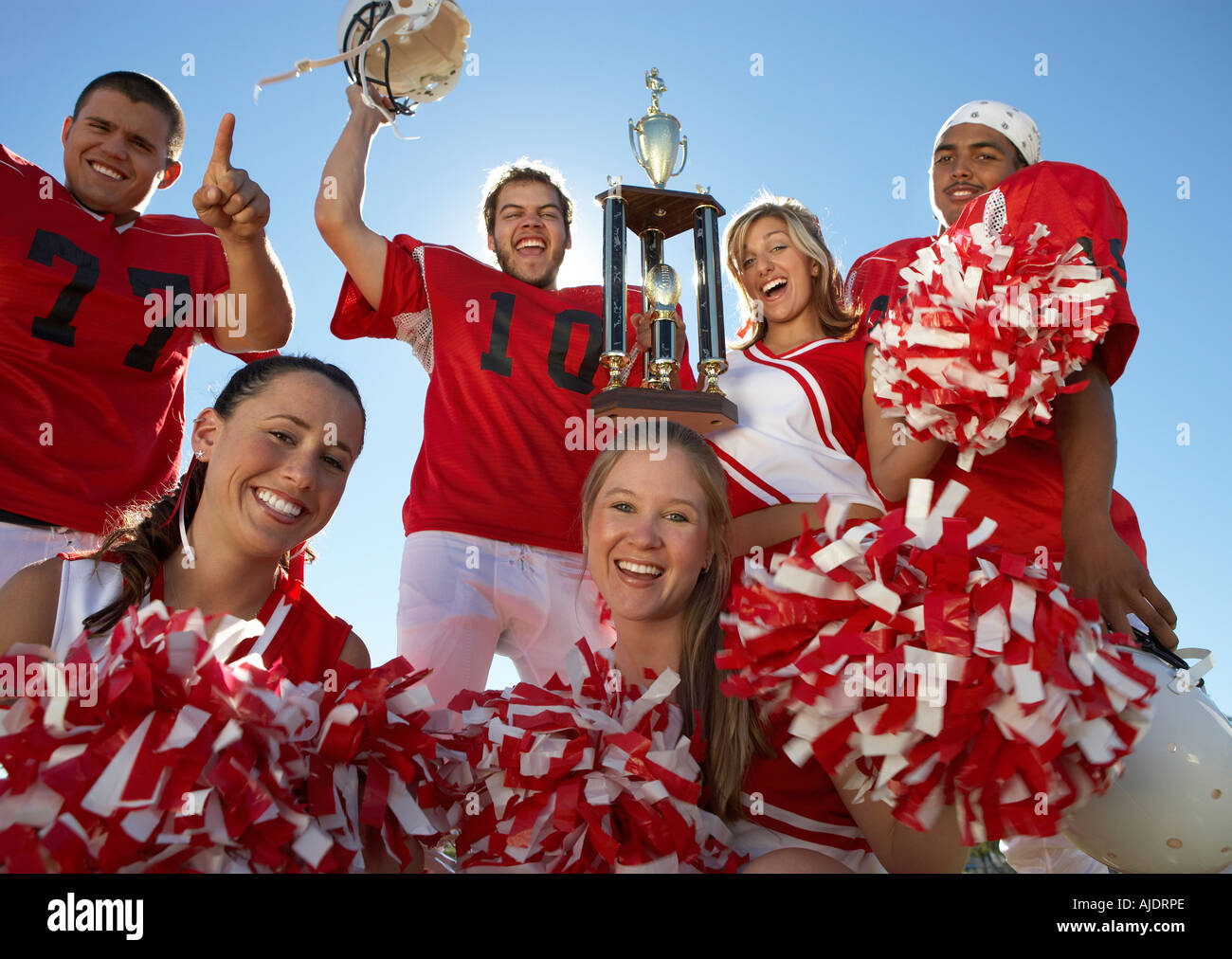 Football players and cheerleaders hoisting trophy, low angle view ...