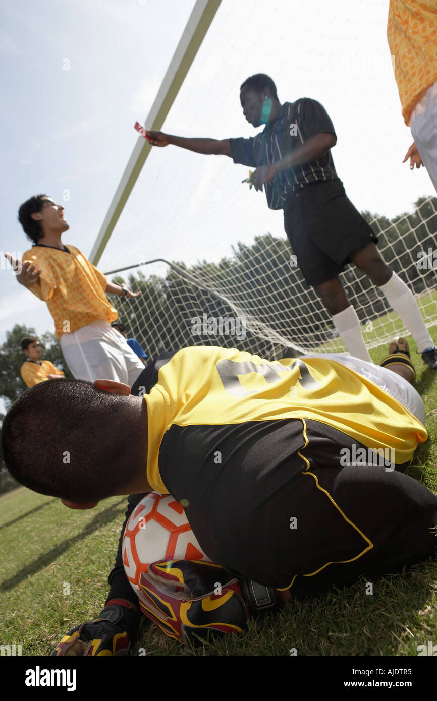Goalkeeper on ground holding soccer ball while referee gives red card ...