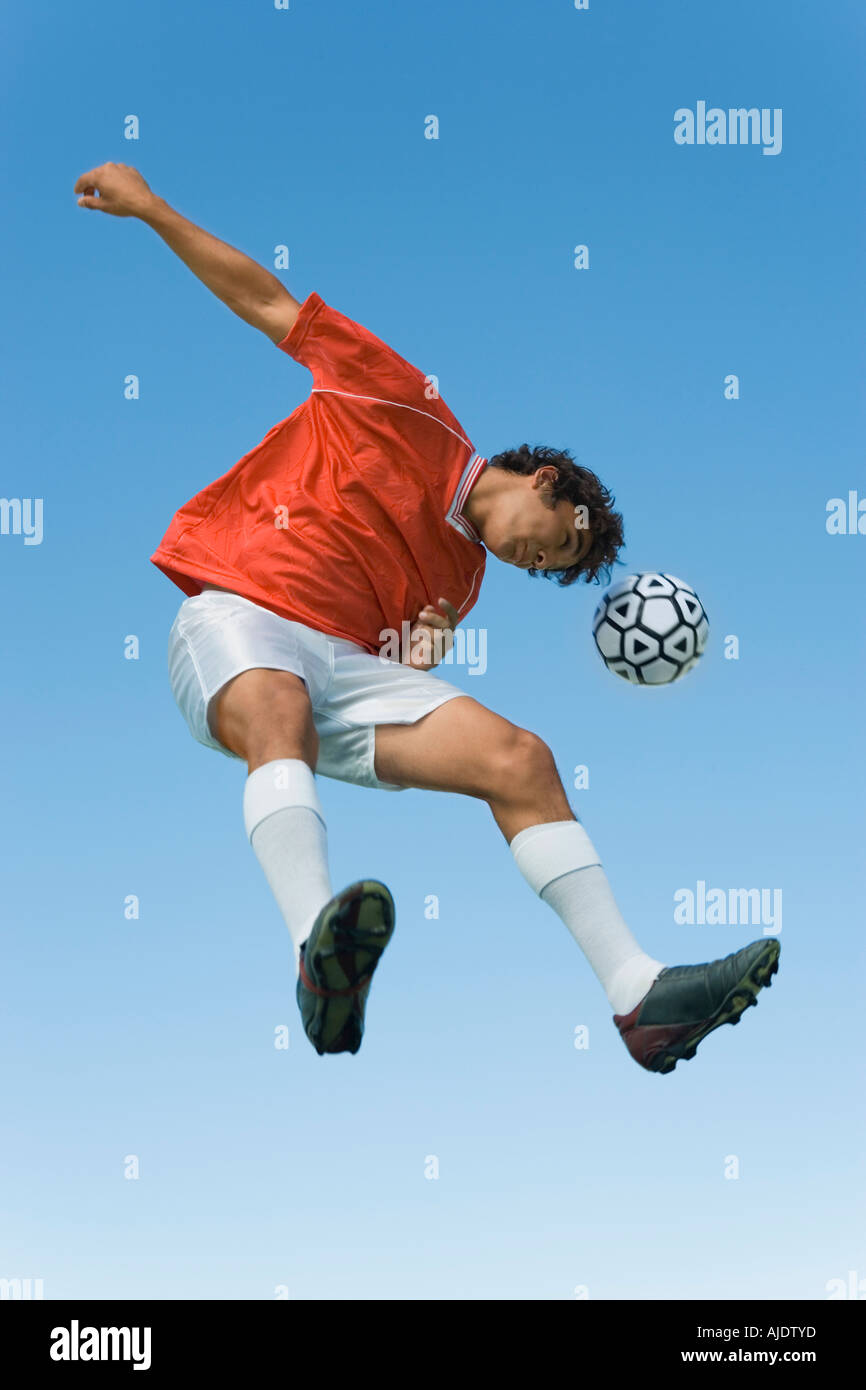 Soccer player jumping to head the ball in mid-air with blue sky ...