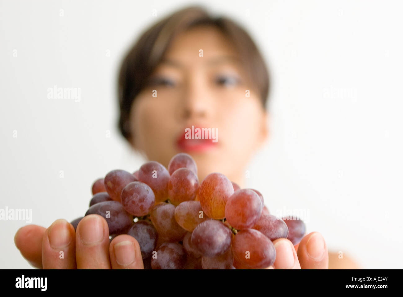 Attractive young Korean Asian woman holding bunch of grapes; focus on grapes Stock Photo - Alamy