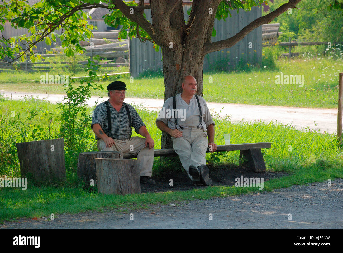 two male workers resting in shade with cool drink. two men sat on bench ...