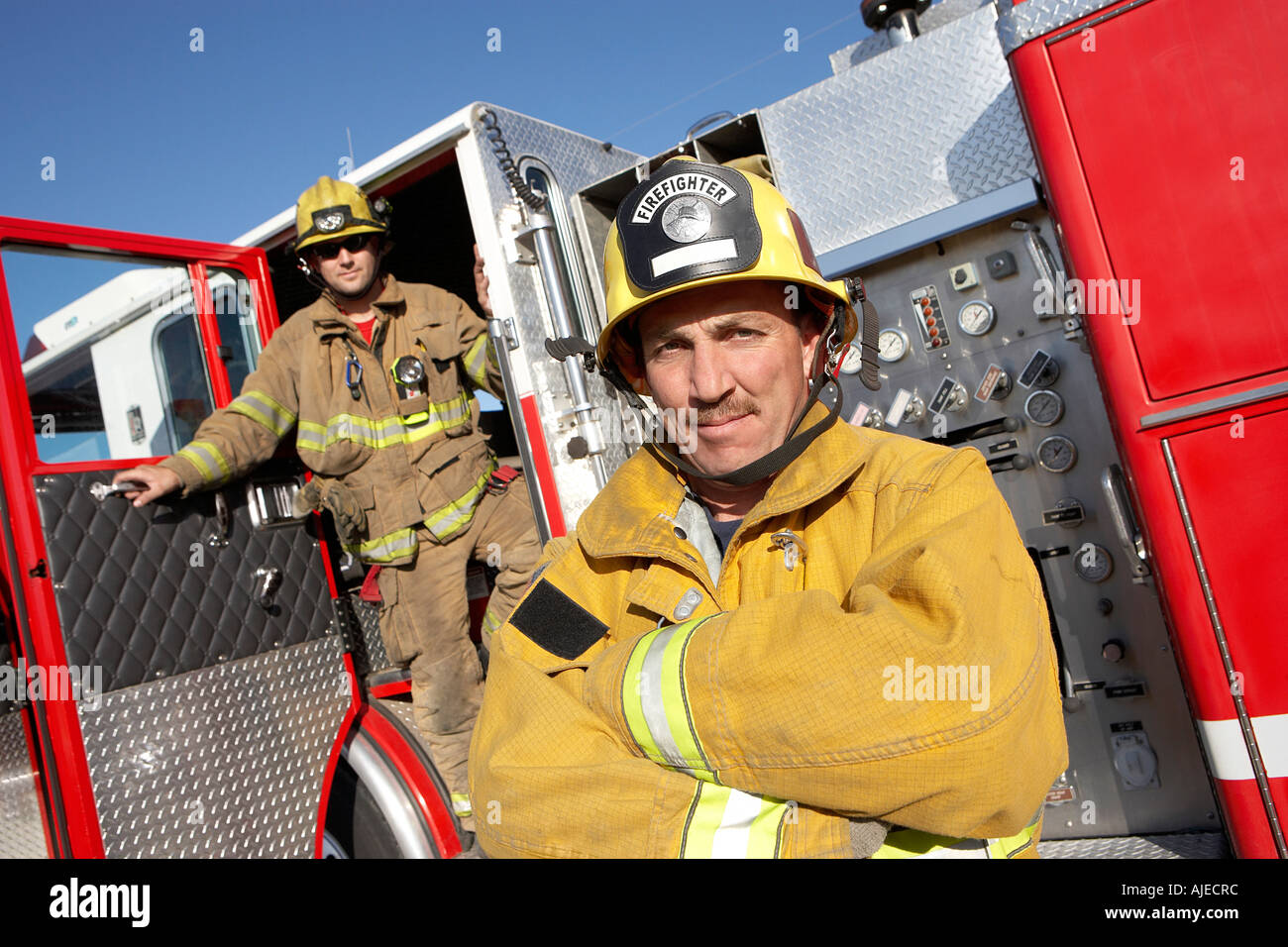 Two fire fighters standing by fire engine Stock Photo - Alamy