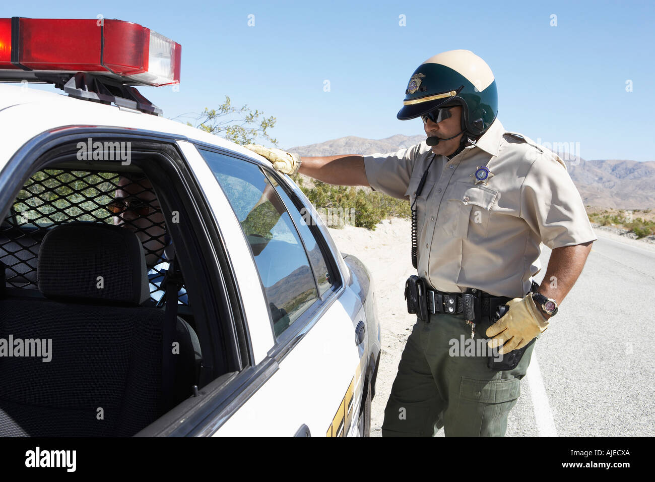 Police officer standing by police car on desert highway Stock Photo - Alamy