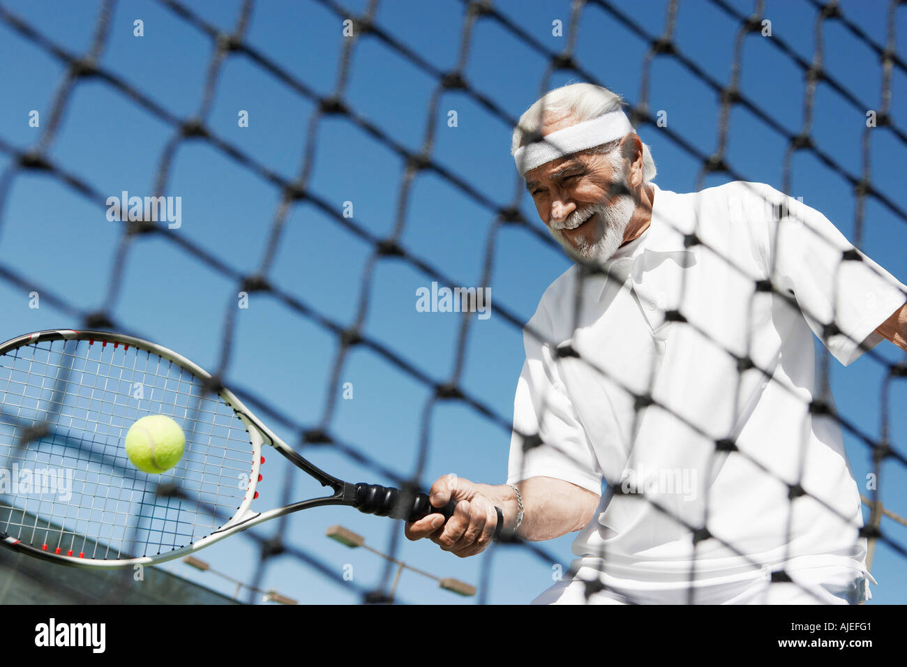 Senior man hitting tennis ball forehand near tennis net Stock Photo - Alamy