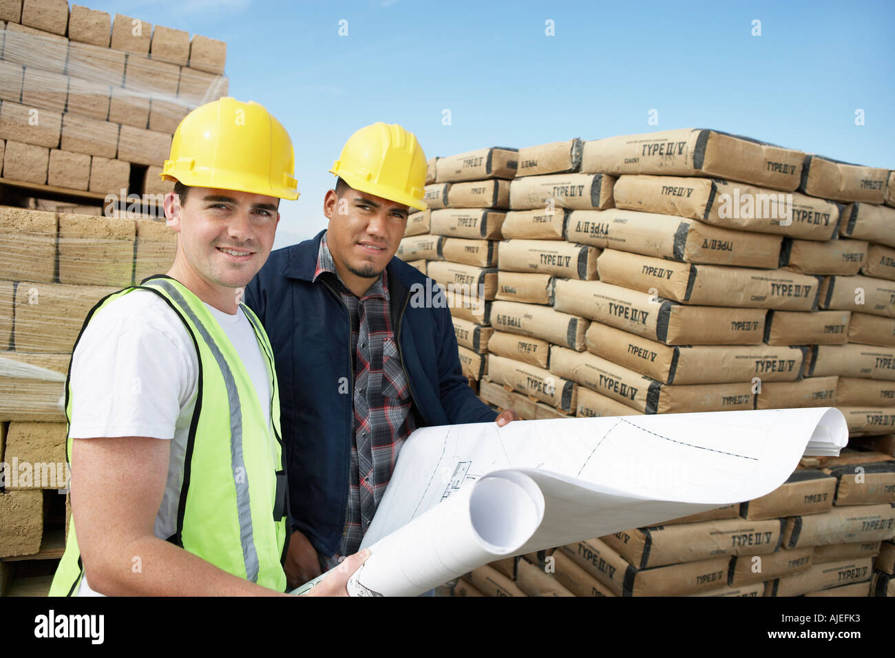Construction Workers standing near supplies, wearing hard hats, looking ...