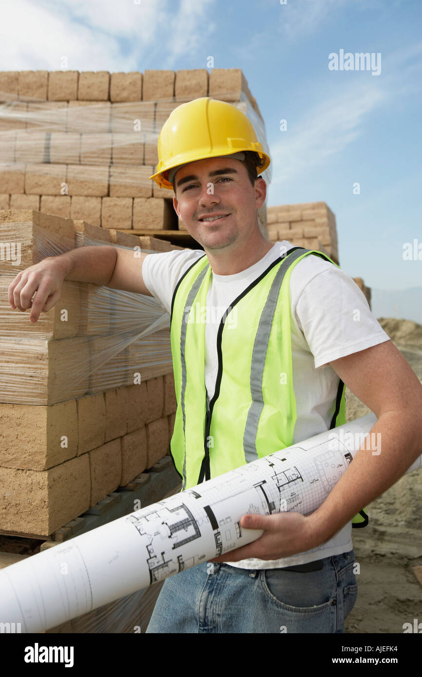 Construction Worker leaning on stack of lumber, holding building plan ...