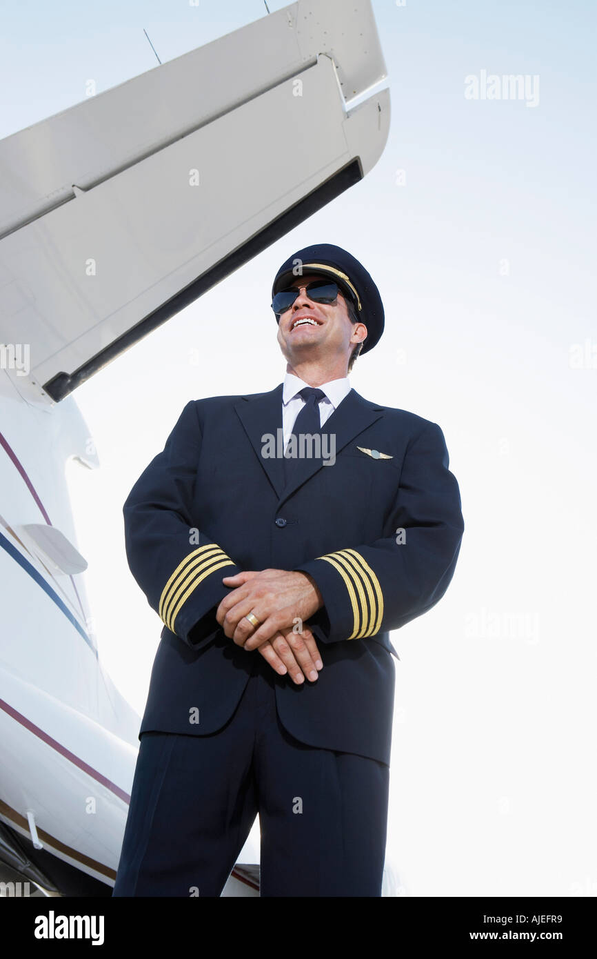 Pilot in uniform standing Beside an Airplane, hands clasped, low angle ...