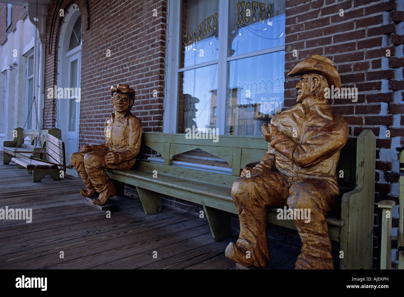 Two old cowboy sculptures sitting on a bench in front of store shops in ...