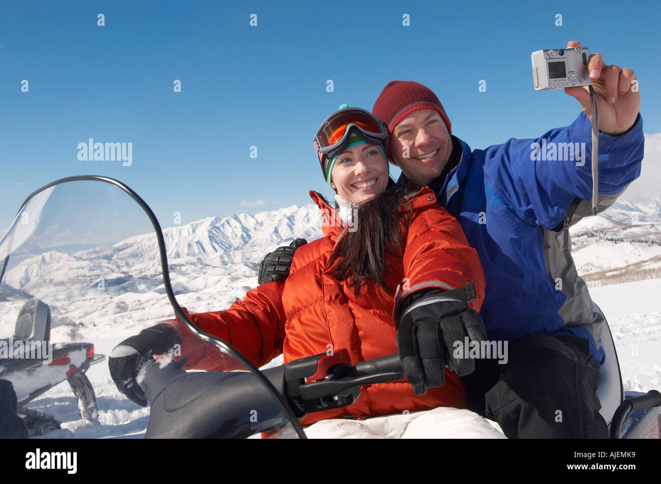Couple sitting on snowmobile in snow, photographing selves with digital ...