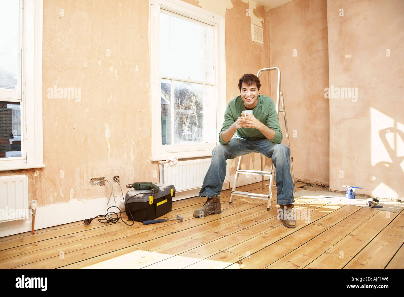 Man sitting on step ladder in unrenovated room Stock Photo - Alamy