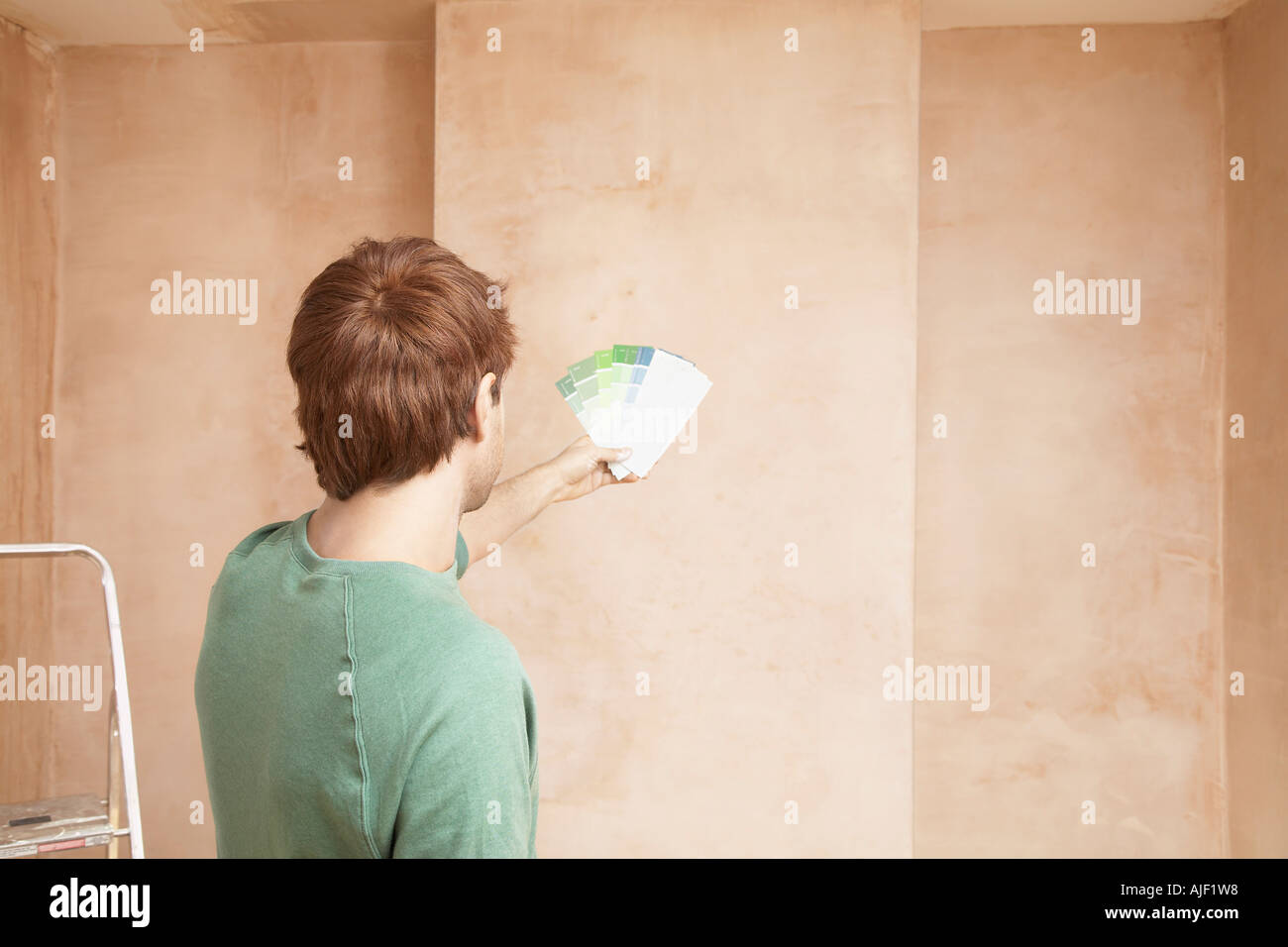 Man looking at paint colour swatches in unrenovated room, back view ...