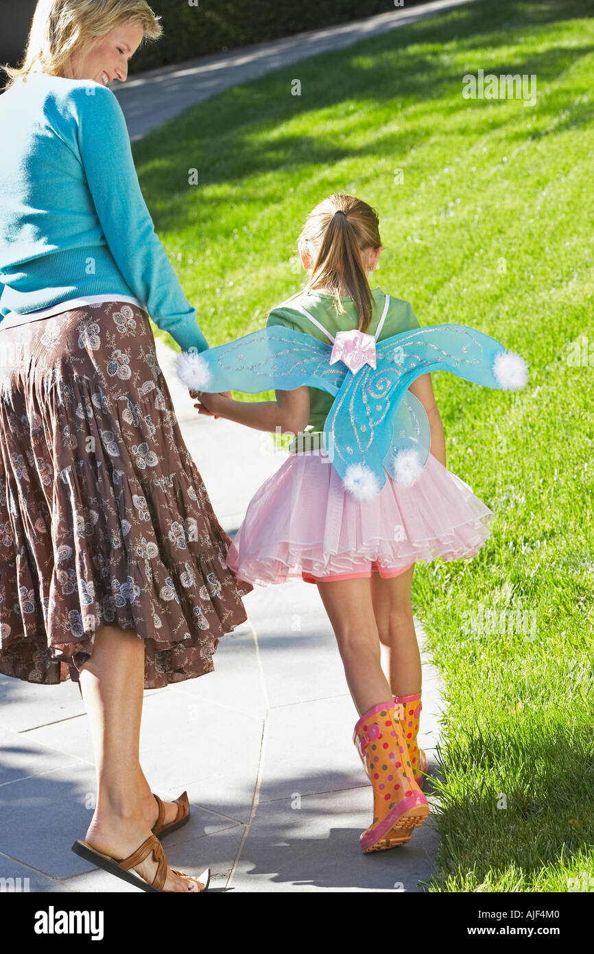 Girl wearing fairy wings and tutu walking with mother on park path ...