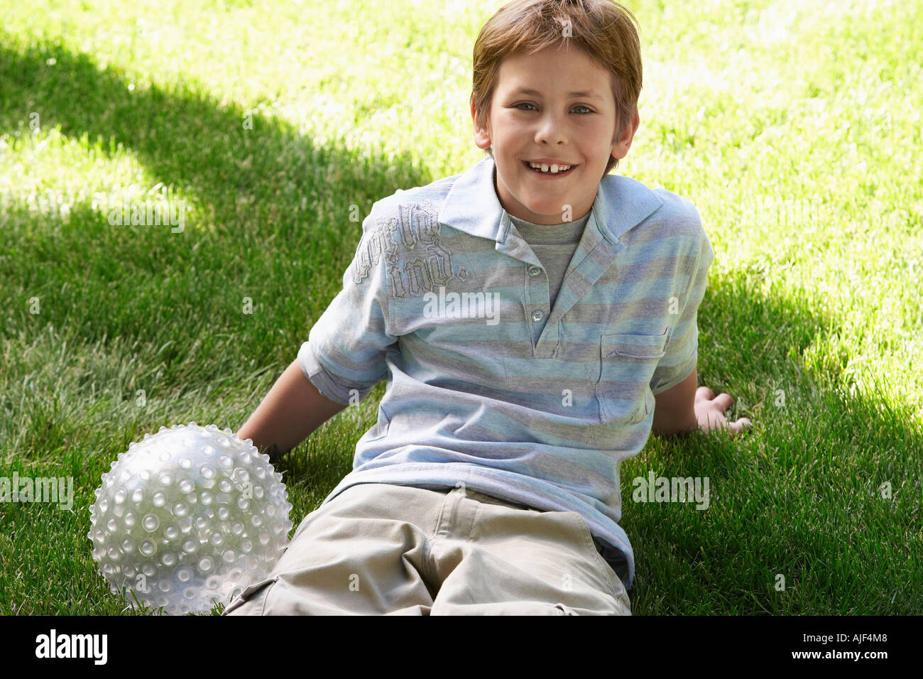 Boy with ball sitting on park lawn, portrait Stock Photo - Alamy