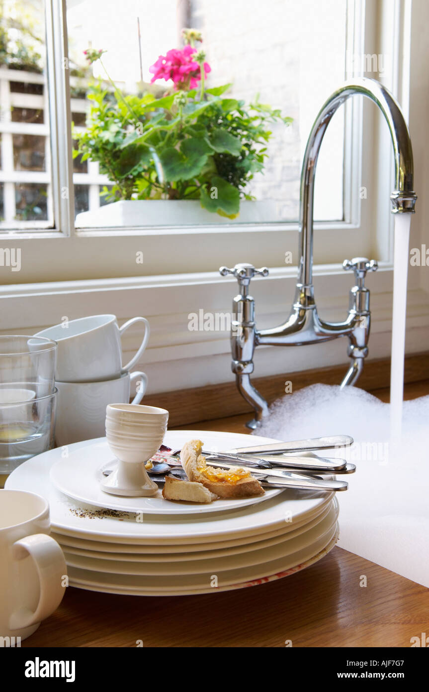 Stack of Dirty Dishes and silverware by Sink with running water below ...