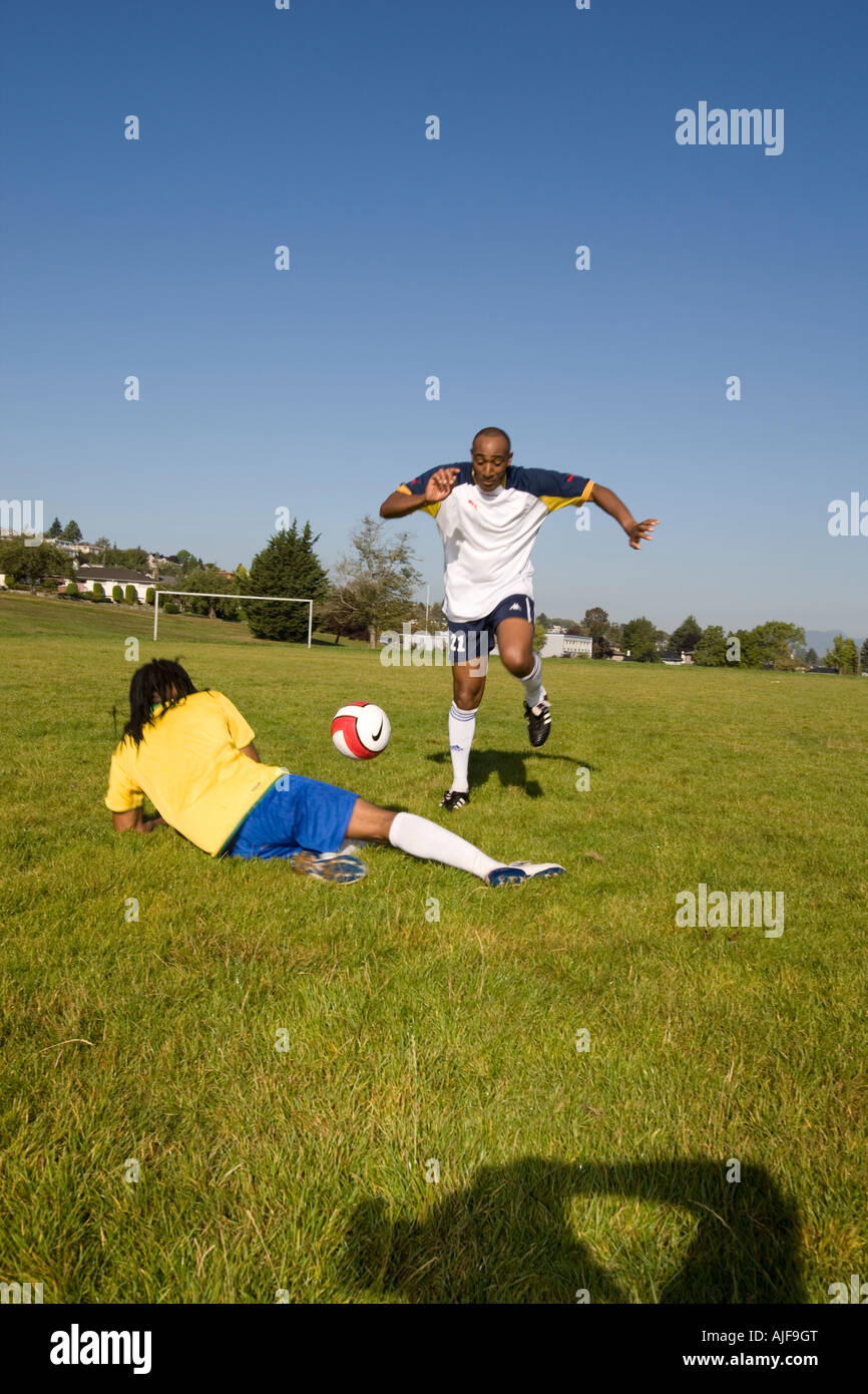 A black African American man playing soccer and slide tackling another ...
