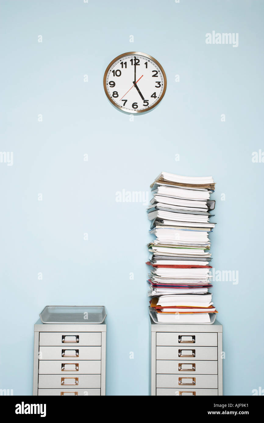 Office wall with clock, stack of paperwork in outbox on file cabinet ...