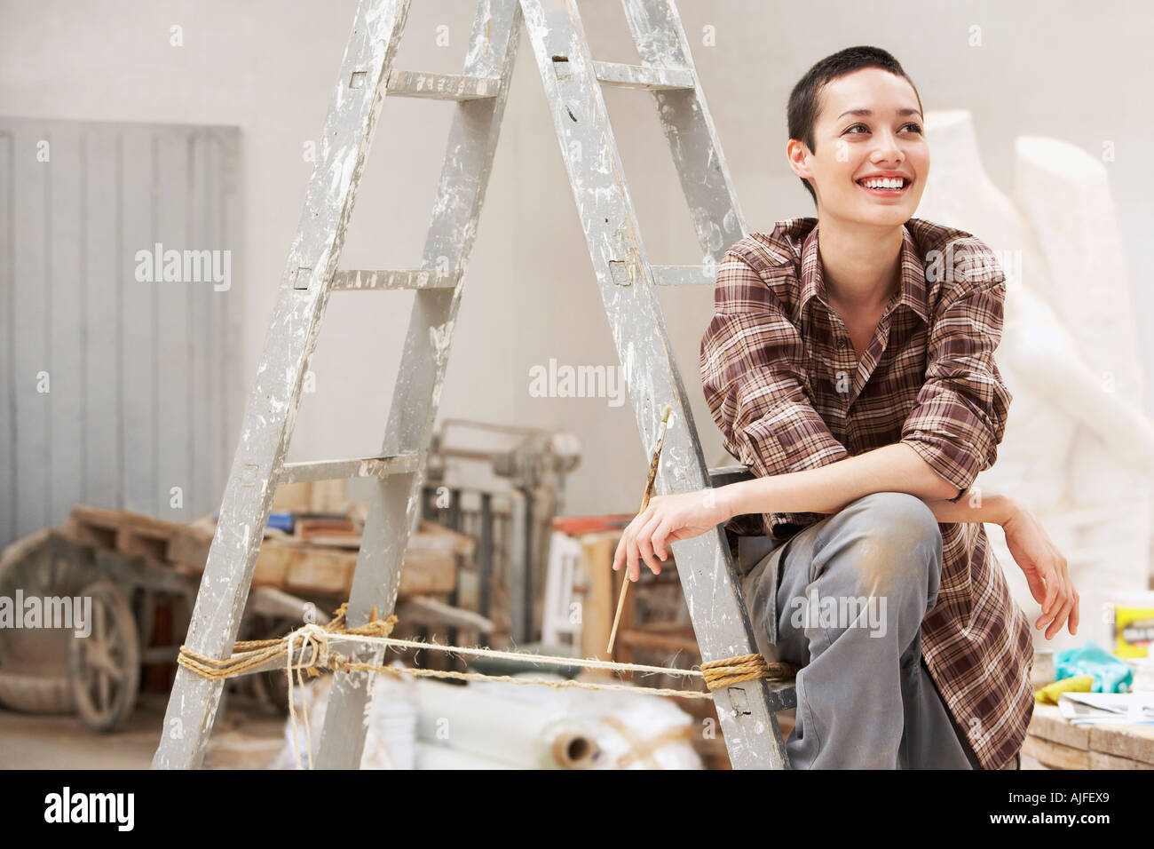 Female Interior Decorator Sitting On Ladder In Work Site Front View