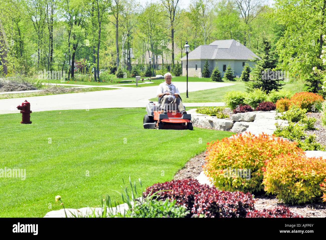 Senior male sitting on his ride-on lawn mower cutting the grass around ...