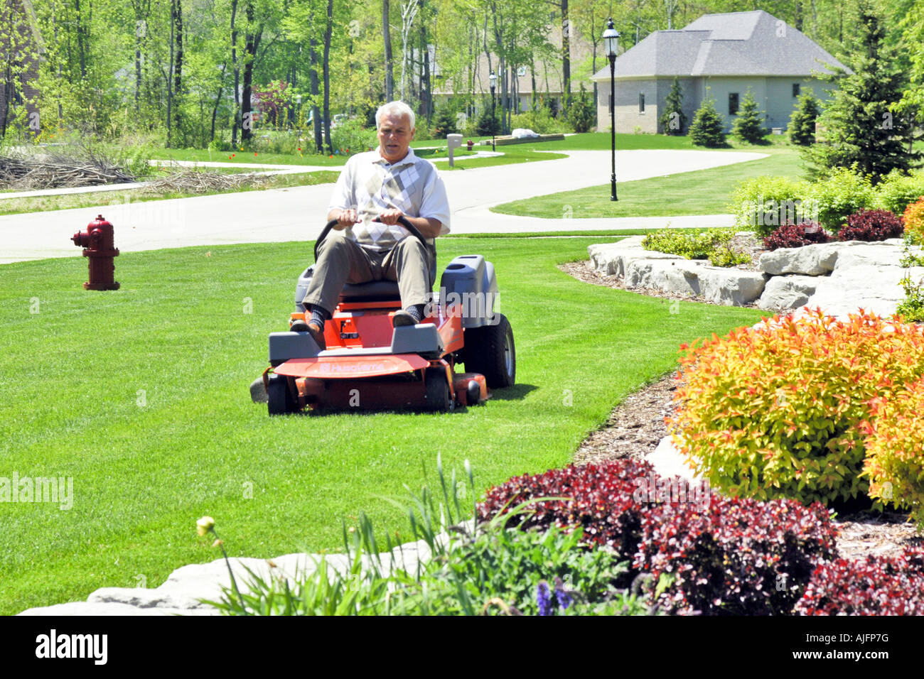 Senior male sitting on his ride-on lawn mower cutting the grass around ...