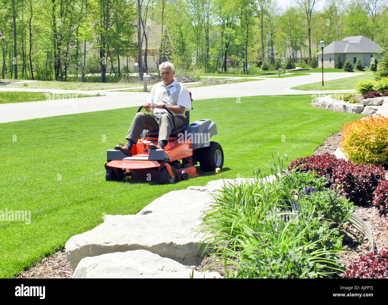 Senior male sitting on his ride-on lawn mower cutting the grass around ...