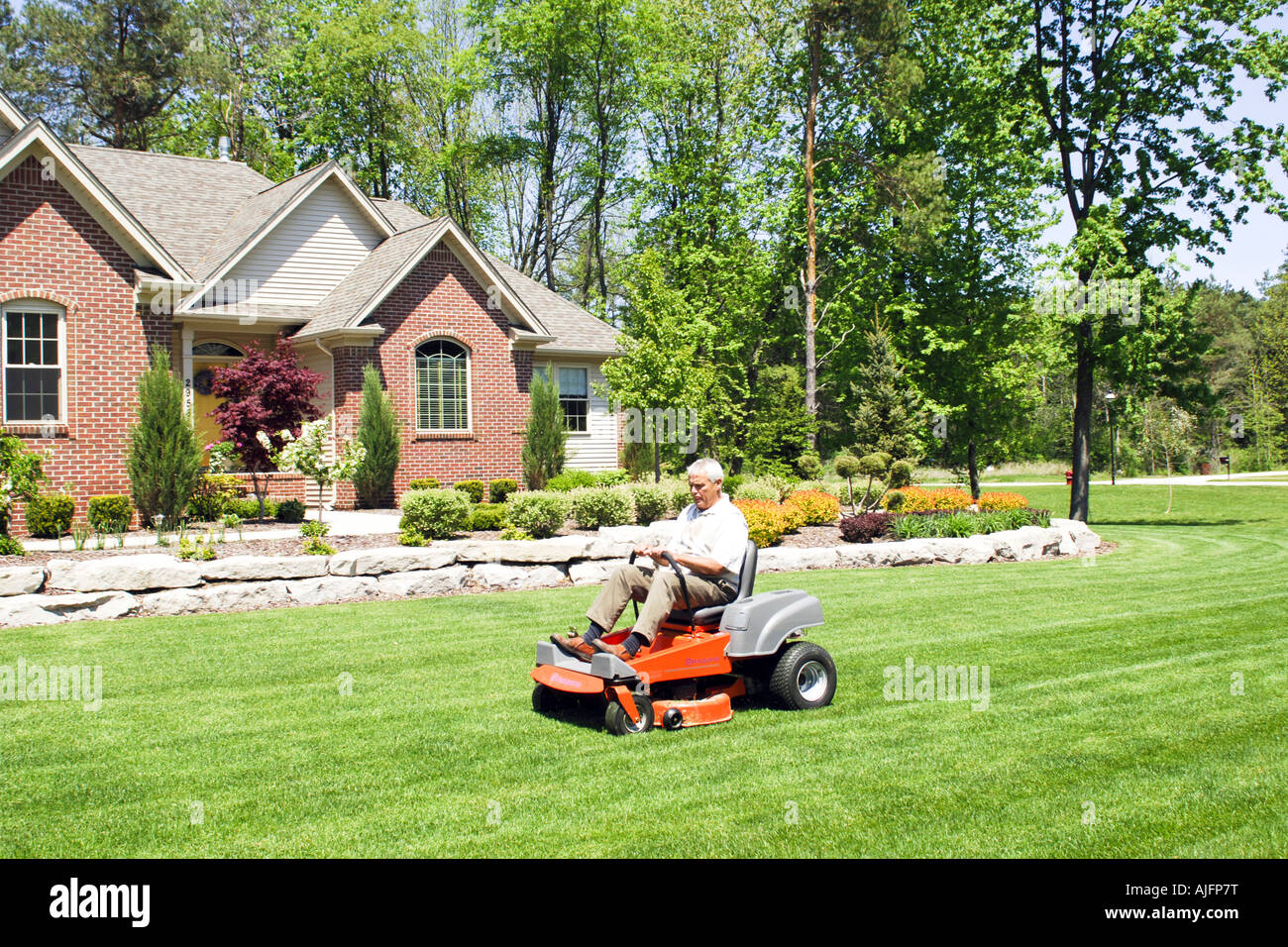 Senior male sitting on his ride-on lawn mower cutting the grass around ...