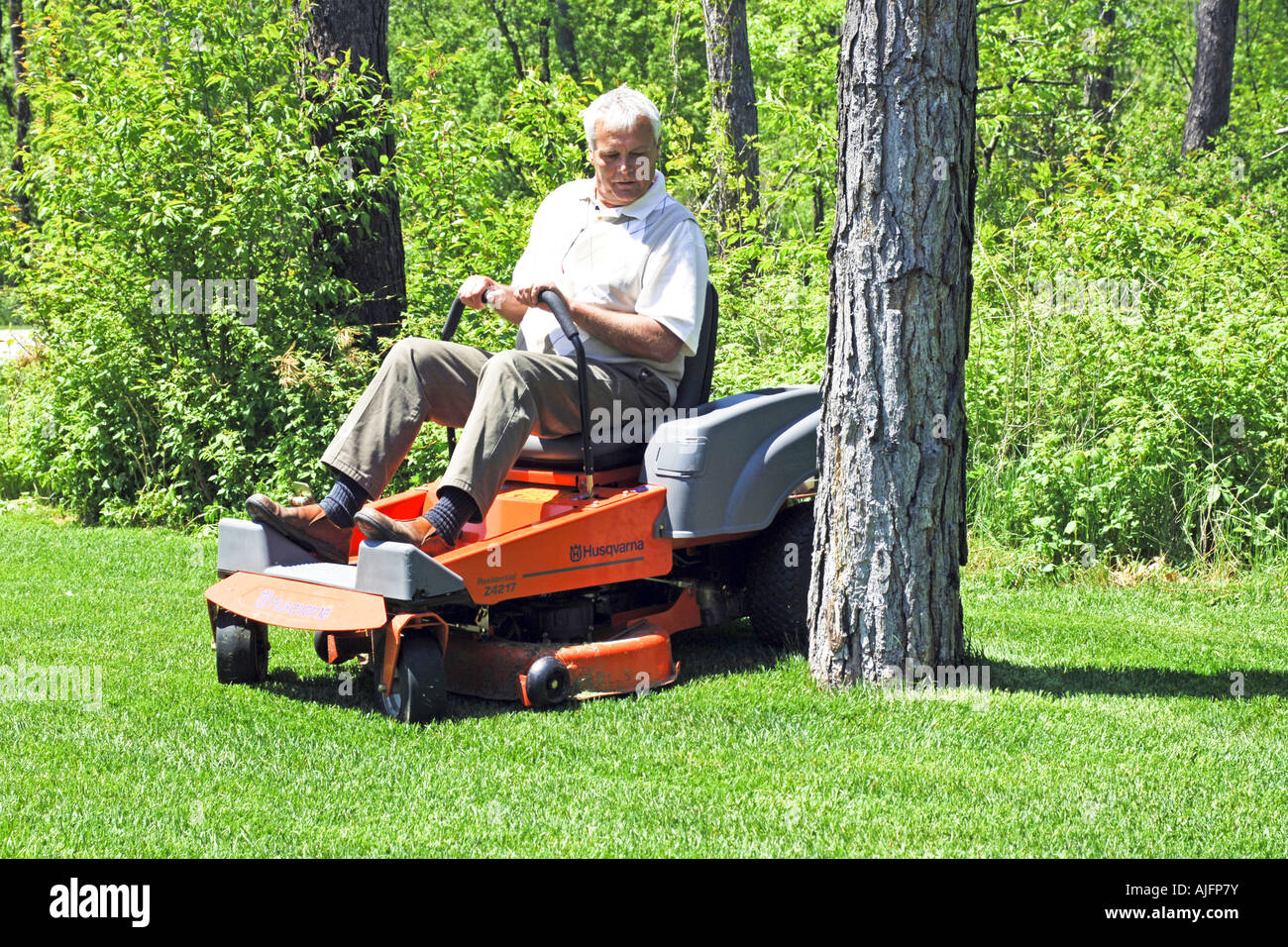 Senior male sitting on his ride-on lawn mower cutting the grass around ...