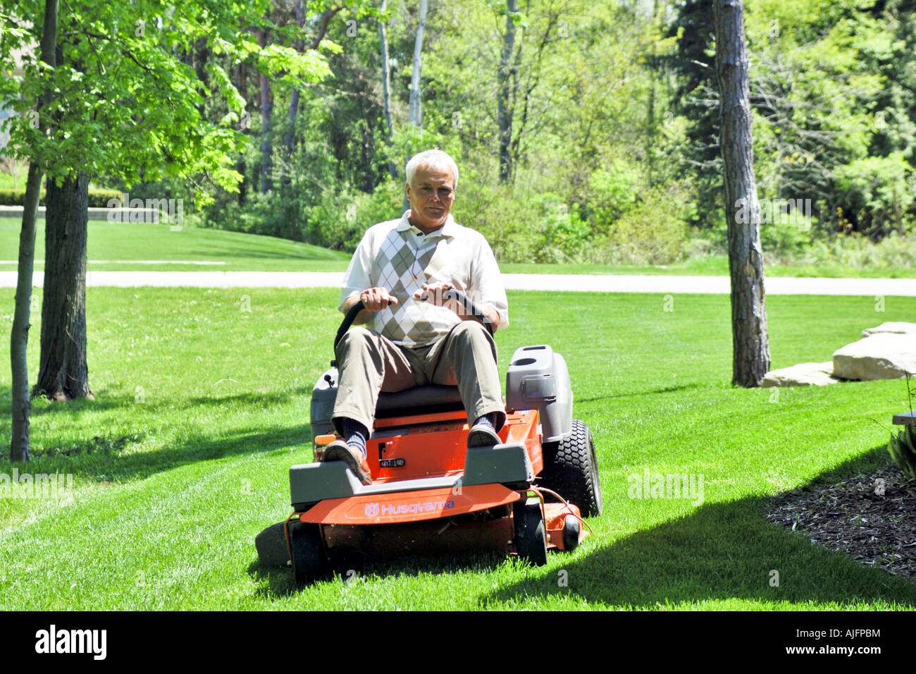 Senior male sitting on his ride-on lawn mower cutting the grass around ...
