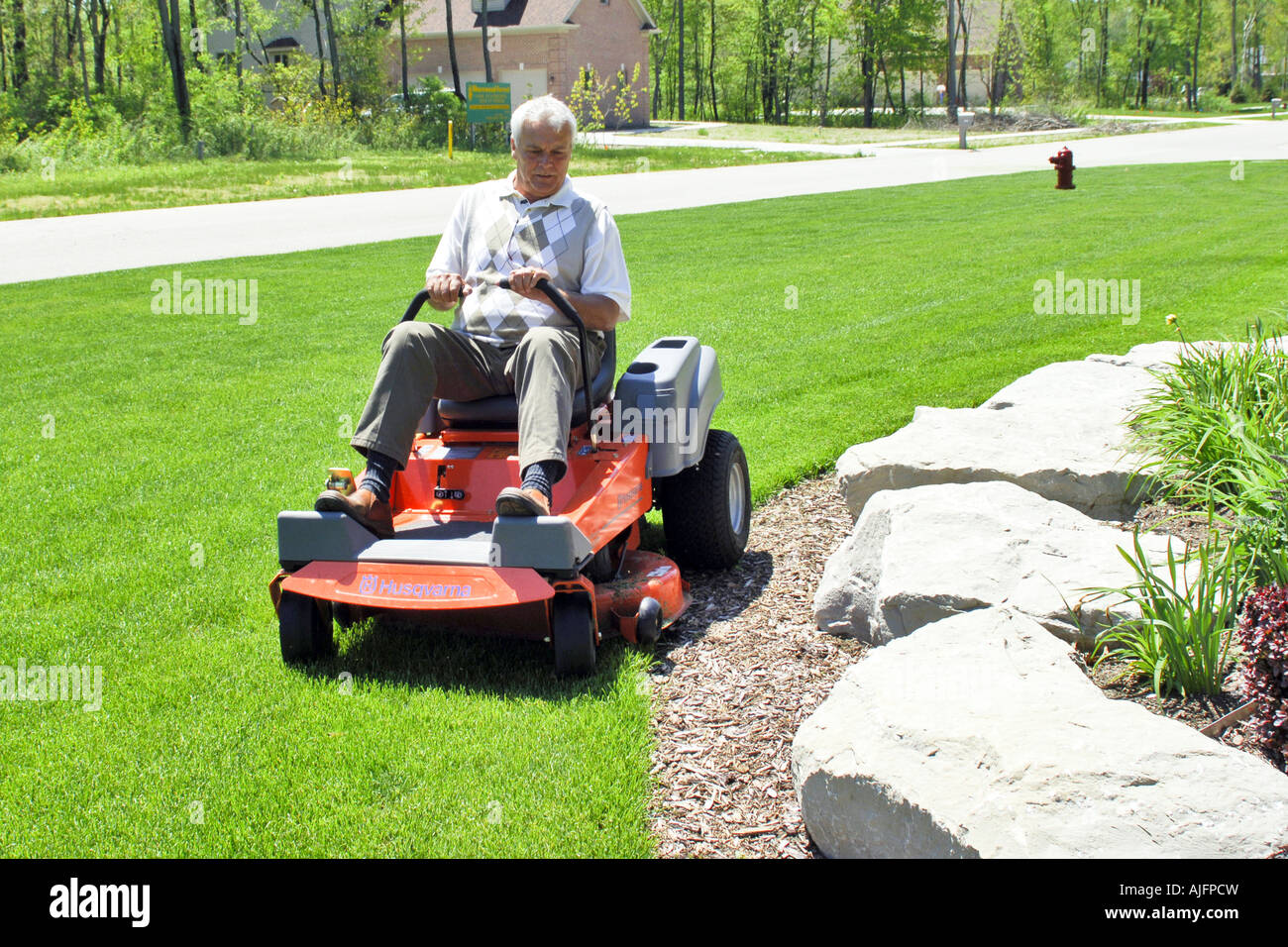 Senior male sitting on his ride-on lawn mower cutting the grass around ...